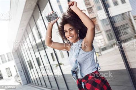 창 근처 의 도시 거리에서 젊은 여성은 쾌활한 춤을 듣고 이어폰을 입고 스마트 폰을 들고 Mp3 플레이어에 대한 스톡 사진 및 기타 이미지 Mp3 플레이어 갈색 머리