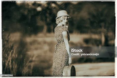 1930 년대의 고전적인 흑인과 백인 사진 패션 여자 드레스와 핸드백과 서 있는 밀 짚 모자 농촌 풍경에 여름 어깨 너머로 찾고 금발 머리에 대한 스톡 사진 및 기타 이미지