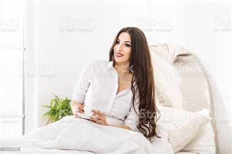 젊은 아름 다운 여자는 아침에 흰색 셔츠에 침실에서 집에서 뜨거운 음료의 찻잔에서 마시는 여자에 대한 스톡 사진 및 기타 이미지 여자 한 명의 여자만 가정 생활