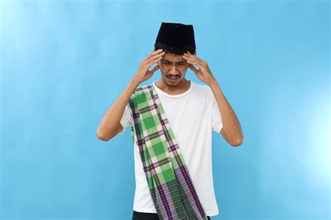 푸른 배경에 고립된 젊은 아시아 남자가 관자놀이를 만지고 두통을 앓고 있습니다 Eid Ul Fitr에 대한 스톡 사진 및 기타 이미지 Eid Ul Fitr 개념