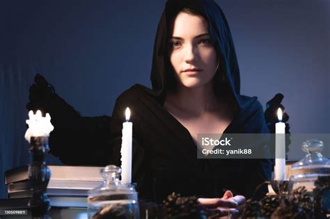 후드와 검은 망토에 아름다운 금발의 초상화 촛불과 책을 들고 카메라를 바라보는 테이블에 앉아 25 29세에 대한 스톡 사진 및 기타 이미지 Istock