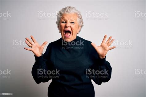 캐주얼 한 검은 스웨터를 입고 고립 된 흰색 배경에 서있는 선임 아름다운 여성은 미친 듯이 미친 소리와 공격적인 표정과 팔을