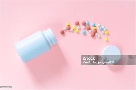 분홍색 배경에 알약과 알약 병 흰색과 오렌지 색상의 둥근 알약은 흰색 플라스틱 알약 병의 분홍색 배경에 쏟아져 맨 위 보기입니다 약용 약품 바이오 해킹 개념 트렌디 한