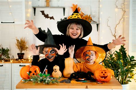 할로윈 축제 의상과 화장을 한 아이들을 둔 엄마는 집에서 부엌에서 호박을 색칠하고 조각하여 모두를 놀라게 함으로써 할로윈을 준비하고 있습니다 10 11세에 대한 스톡 사진