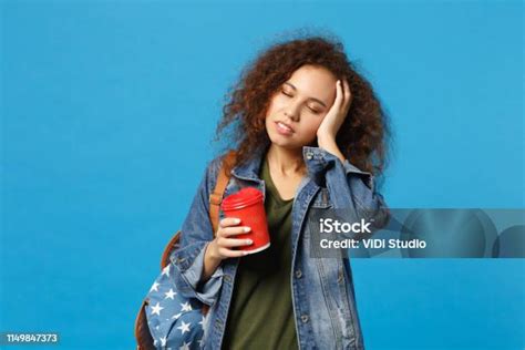 데님 옷에 젊은 아프리카계 미국인 소녀 십 대 학생 배낭 홀드 종이 컵 파란색 배경 스튜디오 초상화에 고립 고등학교 대학 대학 개념에서 교육 복사 공간을 모의 합니다 가방에