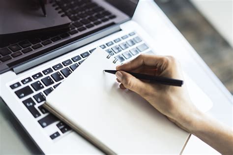 여자는 햇볕이 잘 드는 사무실 비즈니스 및 교육 개념에서 노트북 키보드에 일기에 펜으로 씁니다 클로즈업 시험에 대한 스톡 사진