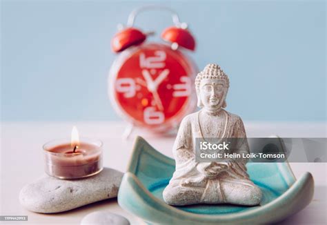자기 관리와 몸의 영혼과 마음 사이의 균형을위한 시간을 찾는 일과 가정 개념 사이의 균형 연꽃은 흰색 색상 앉아 명상 부처님 인형 배경에 빨간 알람 시계 포즈 0명에 대한
