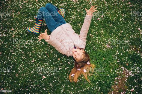 재미 있은 소녀 봄 파크 부드러운 꽃잎 놀고 밝은 녹색 잔디에 누워 비 자 켓을 입고 부츠 아이 들을 위한 계절 패션 4월에 대한 스톡 사진 및 기타 이미지 Istock