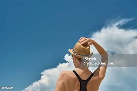 여자는 손으로 머리에 밀짚 모자를 들고 있으며 바다 위의 누적 구름을 배경으로 아름다운 금발의 실루엣을 가지고 있습니다 45 49세에 대한 스톡 사진 및 기타 이미지