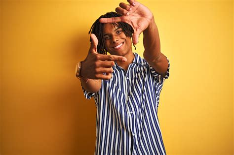 고립 된 노란색 배경 위에 캐주얼 스트라이프 티셔츠를 입고 공포를 가진 아프로 남자는 행복한 얼굴로 손과 손가락으로 프레임을 만드는 미소 창의력과 사진 개념 개념에 대한