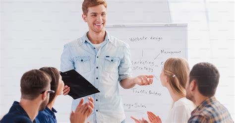 스마트 캐주얼 웨어를 입은 사업가들이 테이블에 함께 앉아 화이트보드 근처에 서서 웃고 있는 동료에게 박수를 보냅니다 사진 Unsplash의 실내 이미지