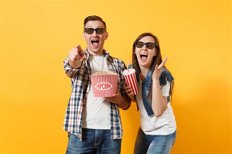 젊은 커플 여자 남자 날짜에 영화 영화를 보고 3d 안경에서 웃 고 소 다 또는 콜라 포인팅 검지 카메라 노란색 배경에 고립의 팝콘 컵의 양동이 개최 극장에서의 감정