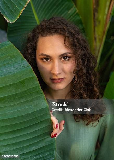 클로즈업 초상화 얼굴 녹색 큰 잎 사이 짙은 웨이브 머리를 가진 아름 다운 젊은 여자 카메라를 들여다 봅니다 위에서 본 모습 20 24세에 대한 스톡 사진 및 기타 이미지