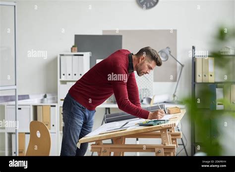 Side View Portrait Of Bearded Architect Drawing Blueprints While Leaning On Desk At Workplace