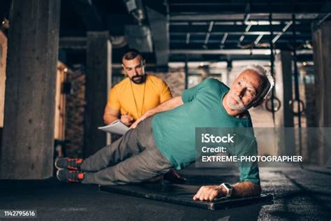 크로스 핏 체육관에서 그를 돕는 자신의 개인 피트 니스 강사와 함께 옆으로 판자 운동을 하 고 적극적이 고 스포티 한 노인 2명에 대한 스톡 사진 및 기타 이미지 Istock
