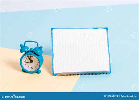 Mini Small Size Alarm Clock Beside A Paper Sheet Placed Tilted Notepaper On The Edge Of Empty