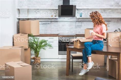 새로운 집에서 테이블에 커피와 골 판지 상자를 풀고 여자 들고 잔의 측면 보기 부엌에 대한 스톡 사진 및 기타 이미지 부엌