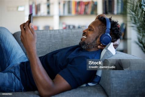 집에서 거실의 소파에 누워 스마트 폰을 사용하는 헤드폰을 가진 웃는 남자 다운로드에 대한 스톡 사진 및 기타 이미지 다운로드