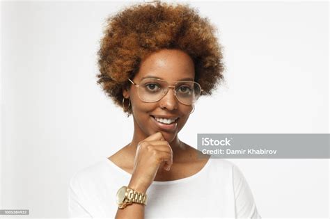 젊은 아프리카계 미국인 여자의 회색 배경에 고립에서 대안을 선택 하는 경우에 그녀의 턱에 손가락을 누르면 즐거운 미소로 카메라를 보고 실내 초상화 갈색에 대한 스톡 사진 및