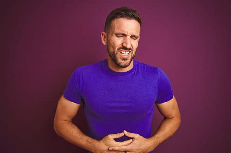 라일락 위에 캐주얼 한 보라색 티셔츠를 입은 청년은 소화 불량 고통스러운 병이 좋지 않기 때문에 위장에 손을 얹고 고립 된