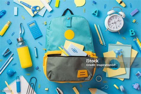 학교 개념으로 돌아 가기 스티커 메모 종이 펜 클립이 흩어져있는 학교 용품 병과 고립 된 파란색 배경에 알람 시계가있는 열린 파란색 배낭의 상단보기 사진 배낭에 대한 스톡