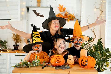 할로윈 축제 의상과 화장을 한 아이들을 둔 엄마는 집에서 부엌에서 호박을 색칠하고 조각하여 모두를 놀라게 함으로써 할로윈을 준비하고 있습니다 10 11세에 대한 스톡 사진