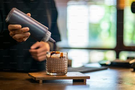 아시아 여성 바리 스타는 카운터의 유리에 거품 우유로 아이스 코코아를 만듭니다 카페에서 고객을 위해 차가운 음료를 준비하는