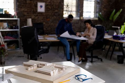 Building Model With Diverse Architects Discussing Blueprints In Background At Office Copy Space