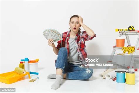 달러 현금 돈의 충격 보유 번들에 여자 흰색 배경에 고립 된 재건축 아파트에 대 한 악기와 함께 바닥에 앉아 있다 벽지 도구를 붙이기 위한 액세서리 집 수리의 개념 개선에