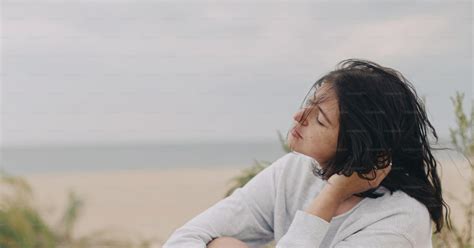 푸른 잔디와 바다를 배경으로 모래 해변에 앉아 바람이 부는 머리를 가진 아름다운 여자 고요한 고요한 순간 해안에서 편안한