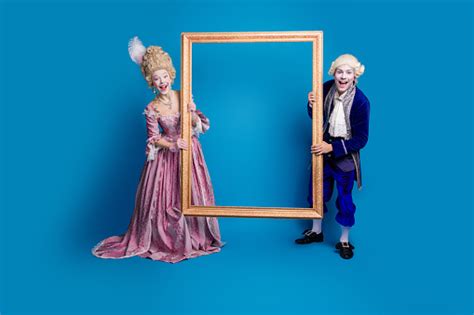 정교한 바로크 양식의 의상을 입은 즐거운 커플이 생생한 파란색 배경을 배경으로 빈 프레임으로 포즈를 취하고 있습니다 16 17 살에 대한 스톡 사진 및 기타 이미지 Istock