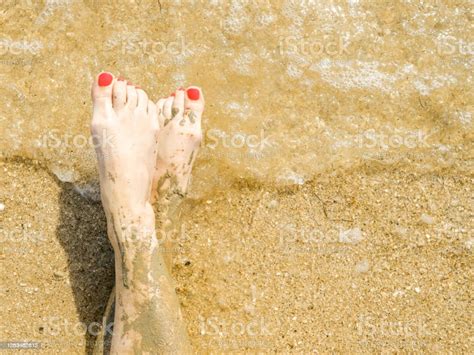 해변의 모래에 밝은 빨간 페디큐어와 아름다운 여성 발의 최고 전망 발의 발목은 약용 진흙으로 얼룩져 있습니다 바다에서 휴식을 취하면서 피부 젊어짐 스파 복사 공간 건강관리와
