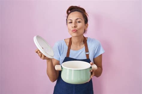 Brunette Woman Wearing Apron Holding Cooking Pot Looking At The Camera
