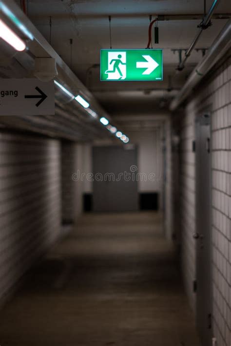 Illuminated Green Exit Sign Hanging From The Wall In And Underground Poorly Lit Corridor Stock