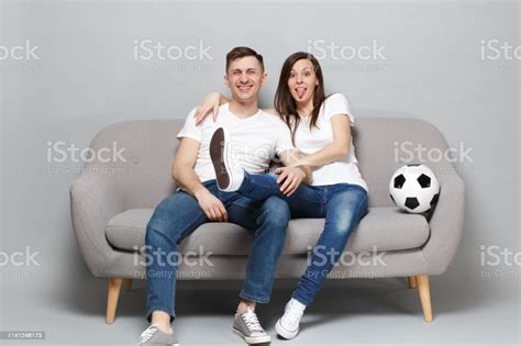 흰색 티셔츠에 명랑 한 커플 여자 남자 축구 팬 응원은 회색 벽 배경에 고립 된 혀를 보여주는 축구 공을 좋아하는 팀 지원 사람들 스포츠 가족 레저 라이프 스타일 개념입니다