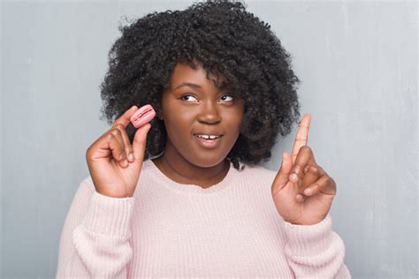 회색 그런 지 동안 젊은 아프리카계 미국인 여자 먹는 핑크 마카롱 아이디어 놀된 벽 또는 행복 한 얼굴 넘버 원 가리키는 손가락 질문 가리키기에 대한 스톡 사진 및 기타