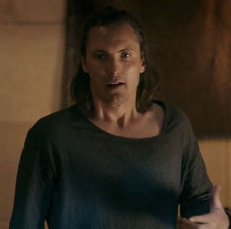 A Man With Long Hair Standing In Front Of A Wall And Holding His Hands Out