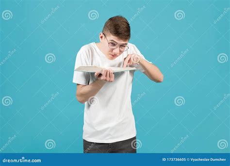 Nerd With Glasses Pointedly Looks At The Camera Holding A Book And Pointing His Finger At It