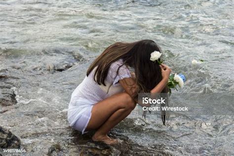 해변에 무릎을 꿇고 긴 물결 모양의 머리에서 꽃 한 송이를 모으는 젊은 여성 꽃 식물에 대한 스톡 사진 및 기타 이미지 꽃 식물 분홍 해변 Istock