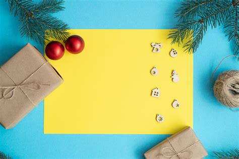 파란색 배경에는 노란 종이 전나무 나뭇가지 빨간 공 선물 상자가 크래프트 페이퍼로 싸여 있고 크리스마스를 위해 집을 장식하기 위한 나무 인형이 있습니다 0명에 대한 스톡