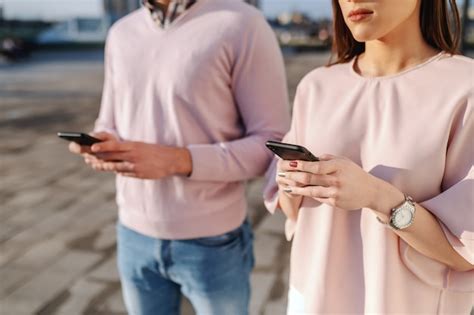 Premium Photo Caucasian Man And Woman Using Smart Phones While Standing Side By Side Outdoors