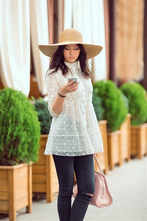 Стильная молодая азиатская девушка с Smartphone на улице города против фасада кафа Стоковое Фото