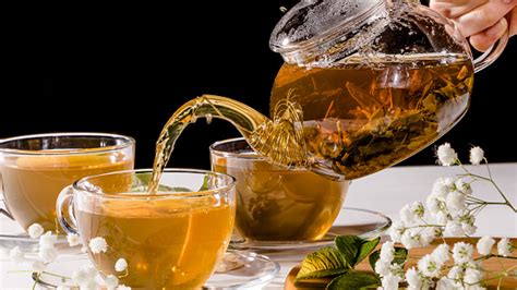 찻주전자에서 양조한 녹차를 머그잔에 붓습니다 차 파티 다도 선 스타일의 전통 녹차 한 잔과 주전자 과일 슬라이스와 꽃 차 다도